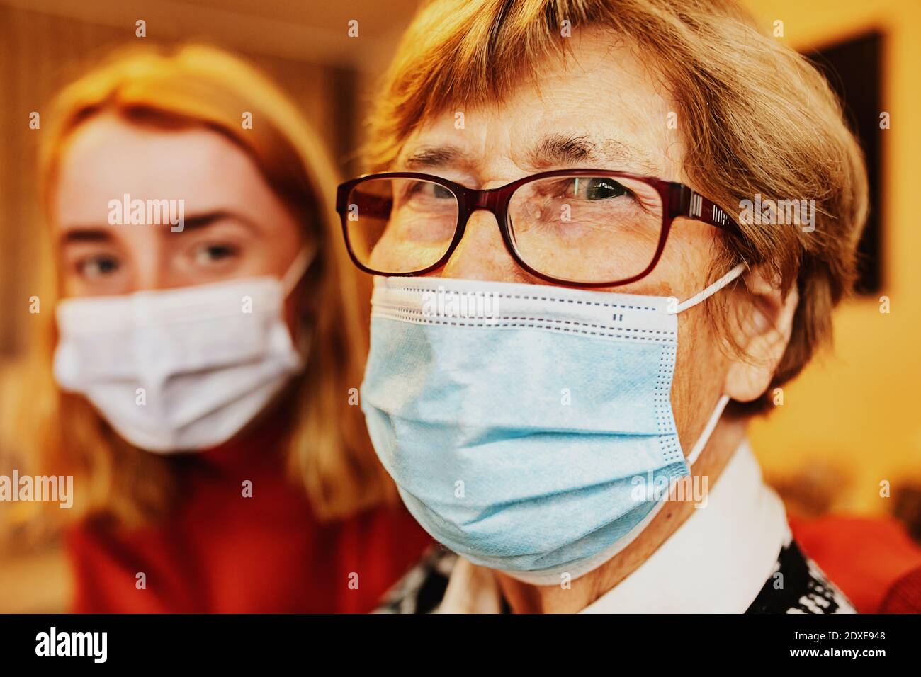Grandmother wearing face mask and eyeglasses staring while sitting by ...