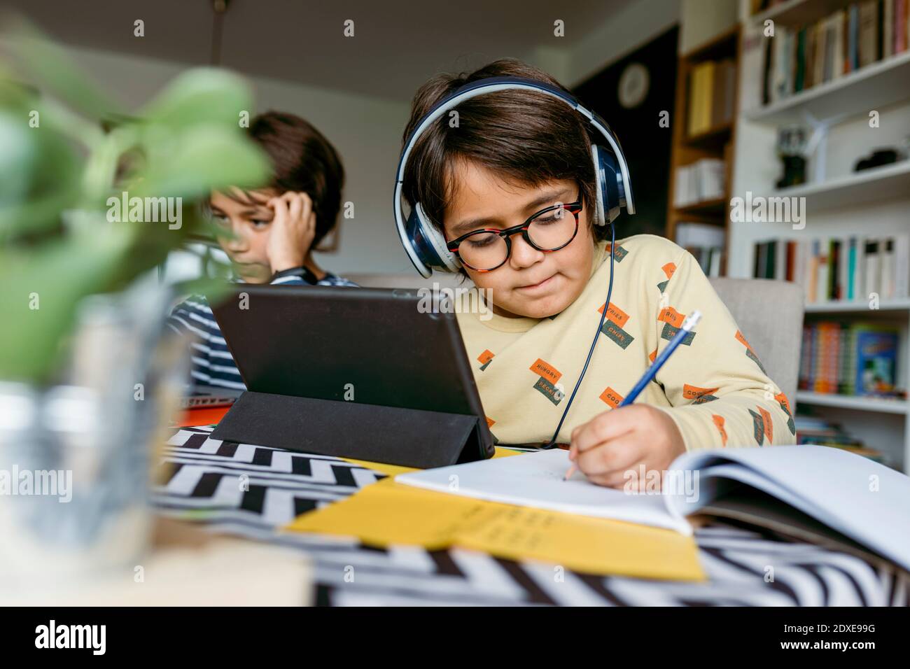 Boy writing notes through digital tablet sitting with male friend ...