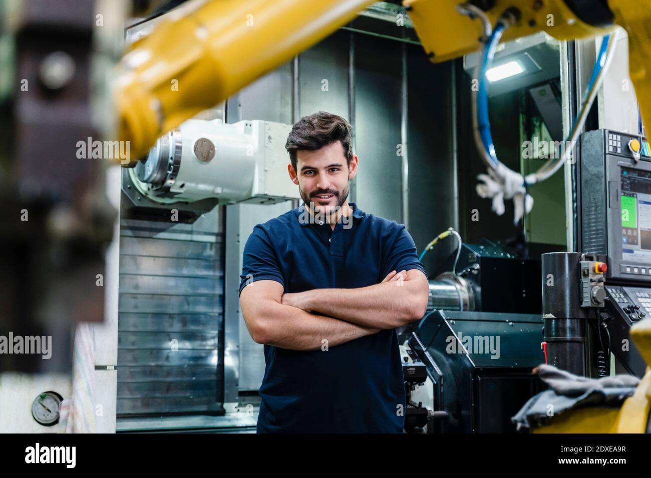 Male manual worker with arms crossed smiling while standing in factory ...