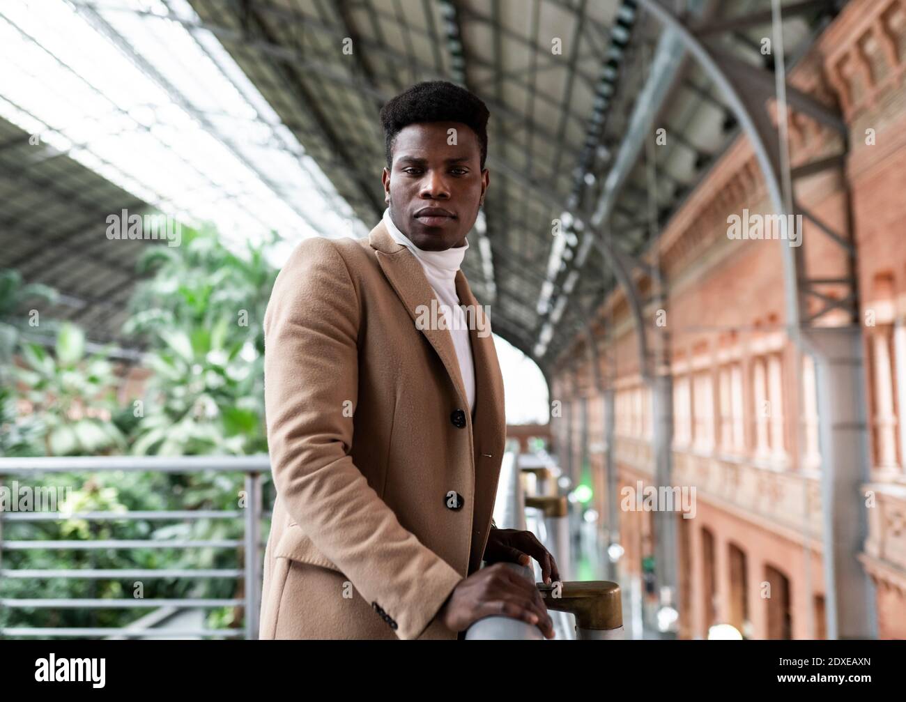 Young man standing by railing at station Stock Photo - Alamy