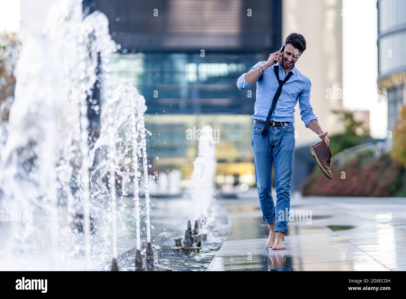 Smiling businessman talking on mobile phone holding shoe while walking ...