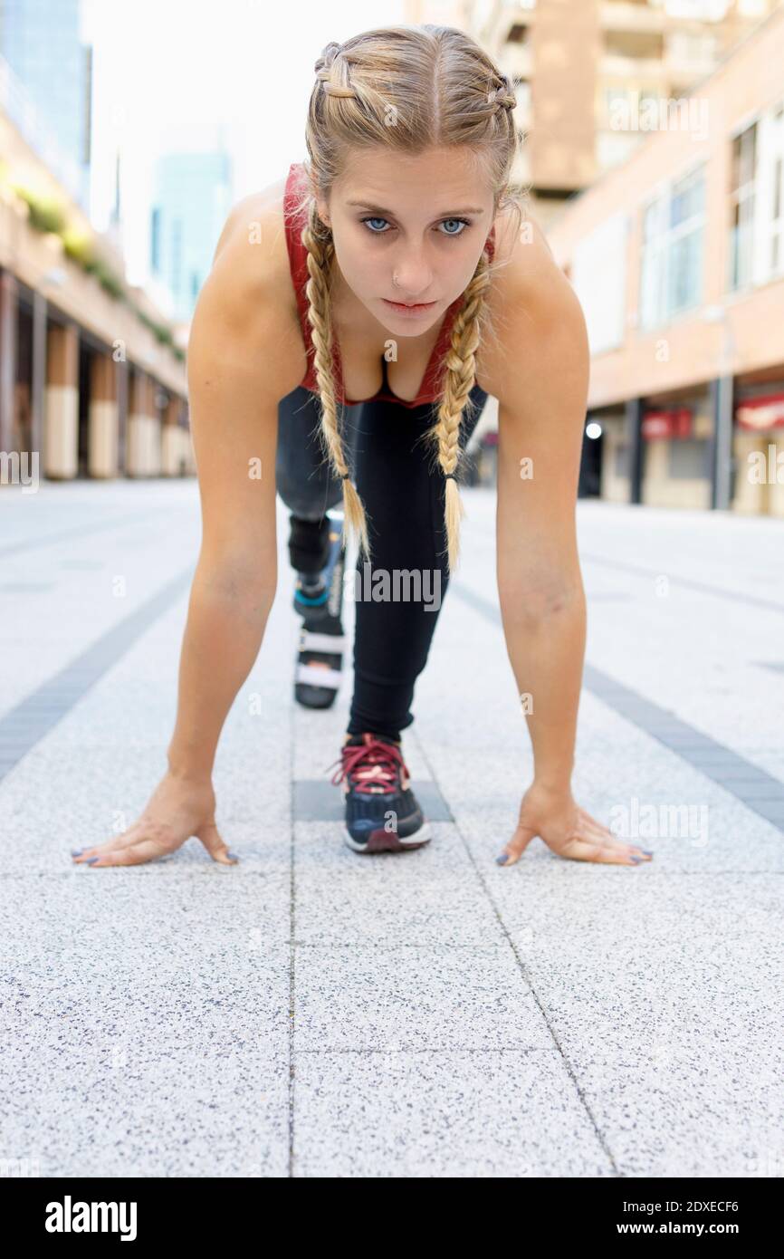 Young woman with prosthetic leg crouching for sports race on footpath ...