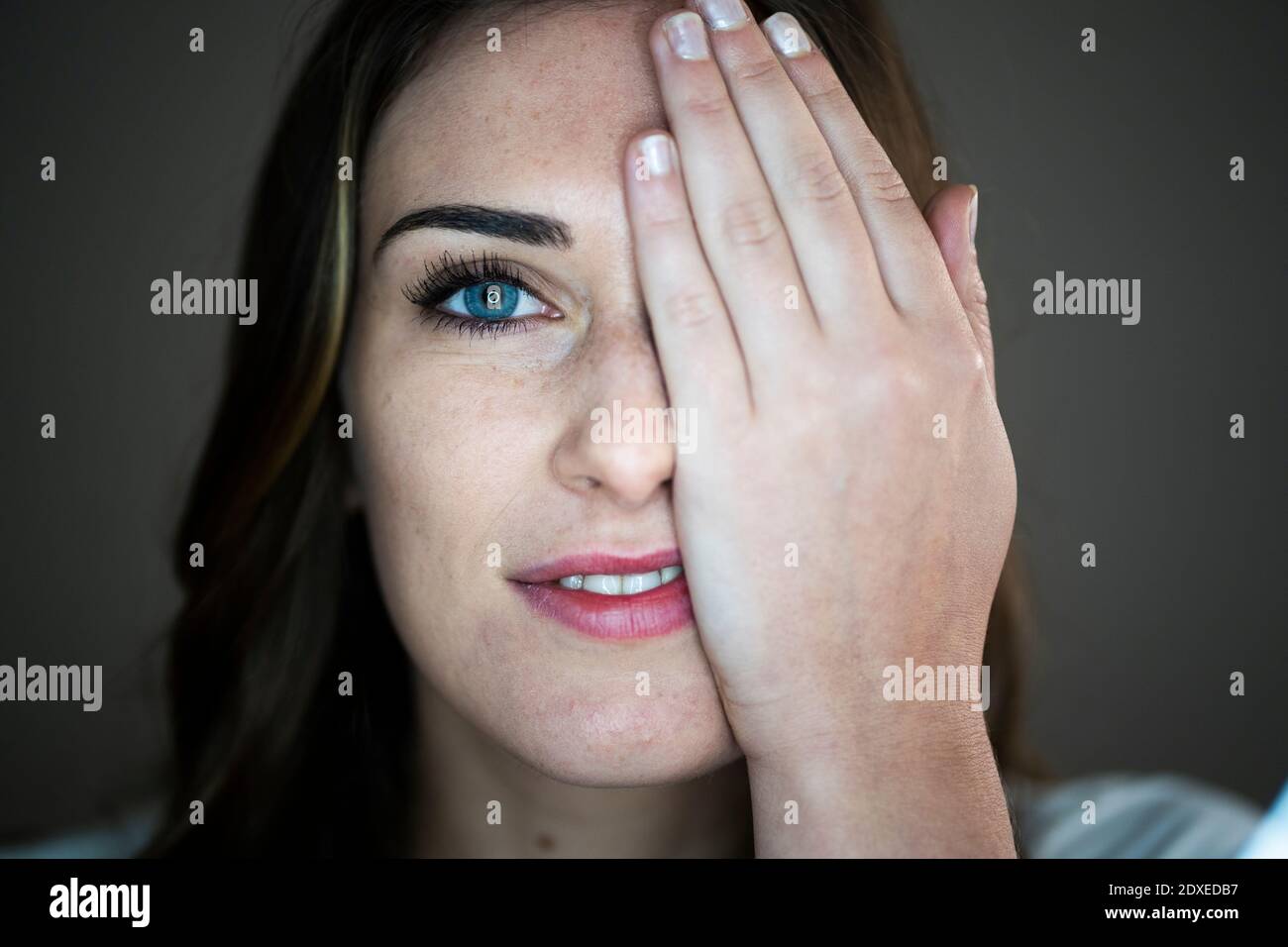 Young woman covering hand over eye at studio Stock Photo - Alamy