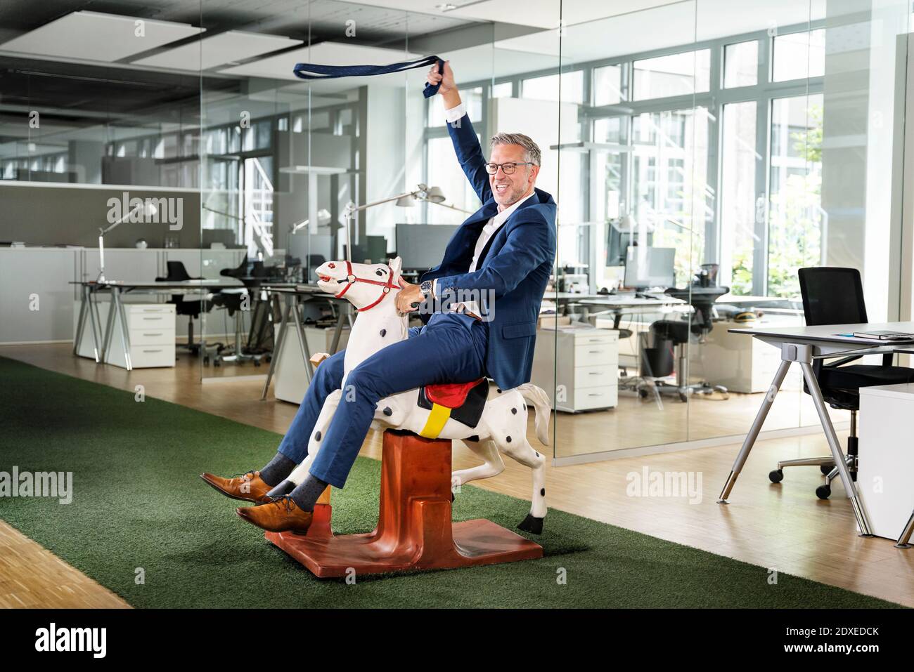 Playful male professional pretending to ride rocking horse at office ...