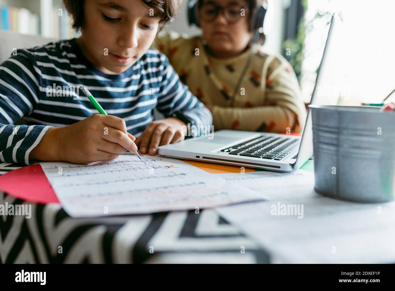 Boy completing homeschooling assignment while male friend sitting ...