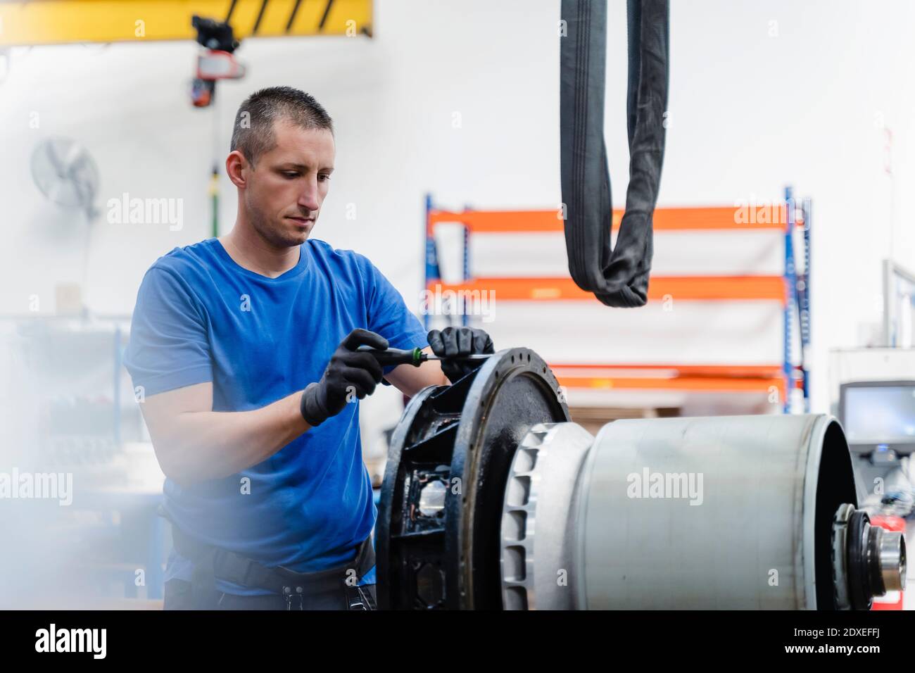 Male technician repairing machine while standing at illuminated factory ...
