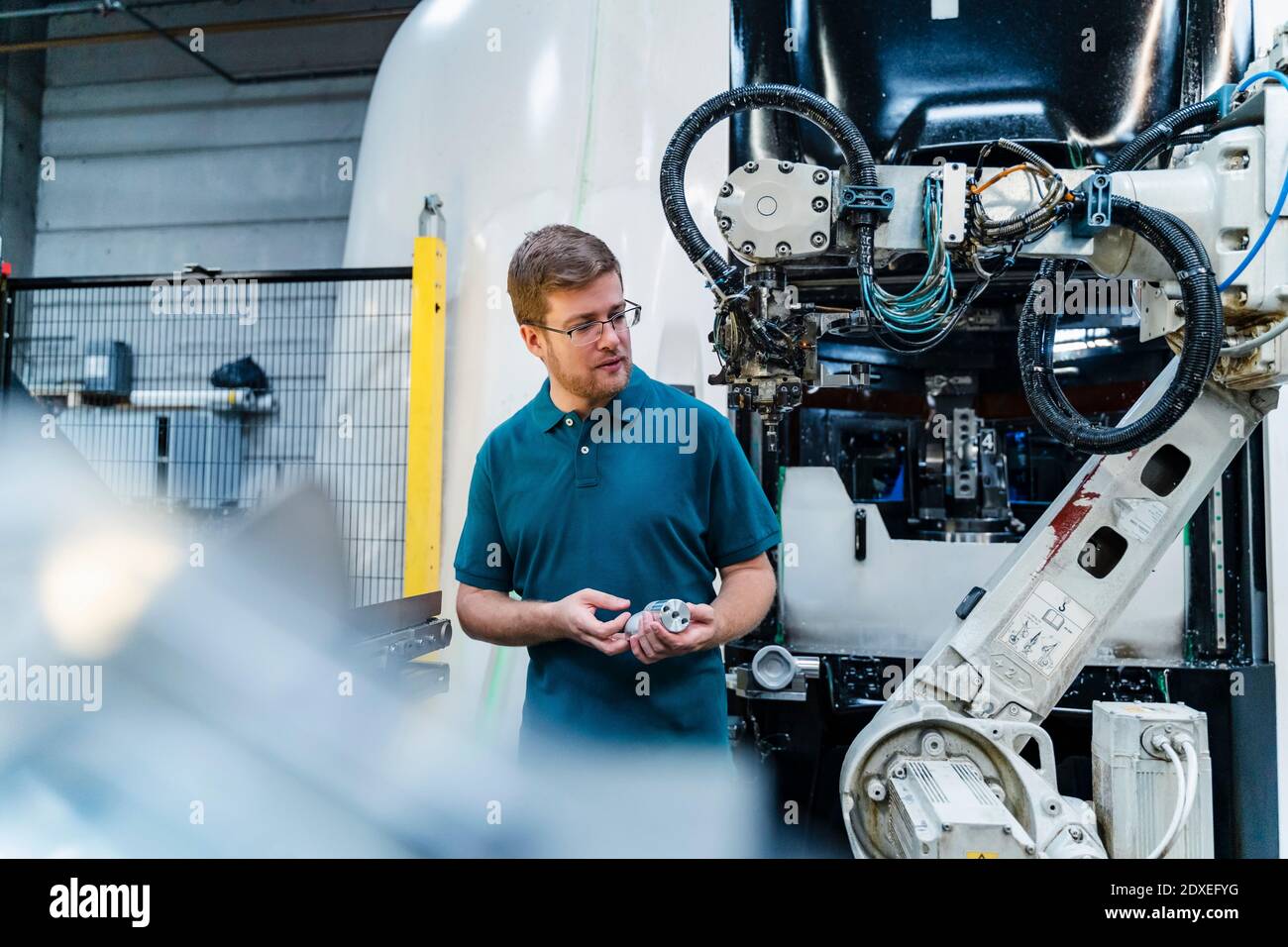 Male manual worker looking at robotic arm while holding machine part at ...