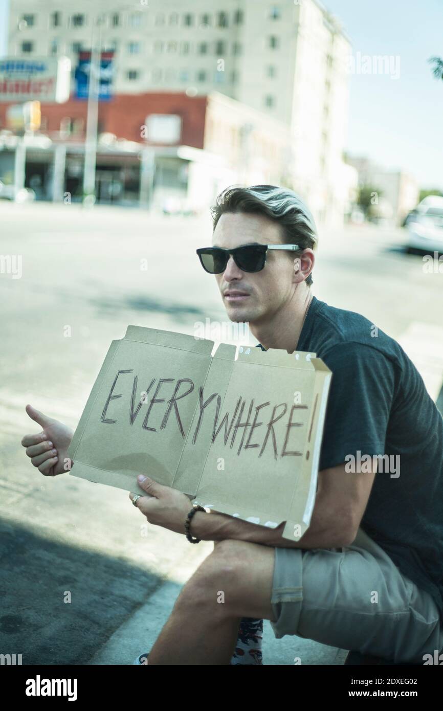 Handsome man sitting with signboard on sidewalk Stock Photo - Alamy