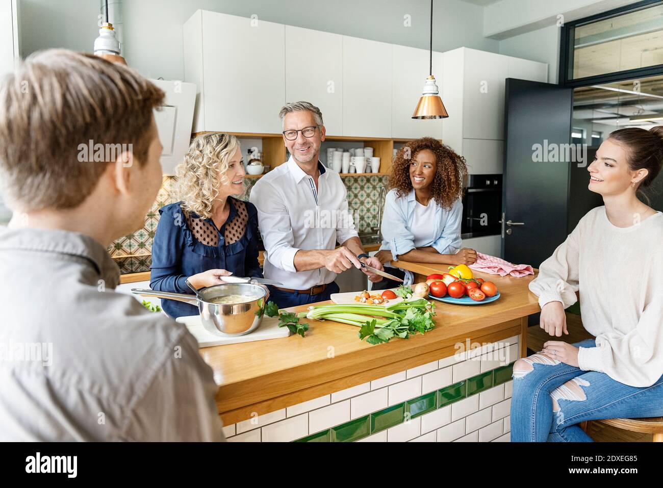 Smiling business colleagues talking while cooking in office kitchen ...
