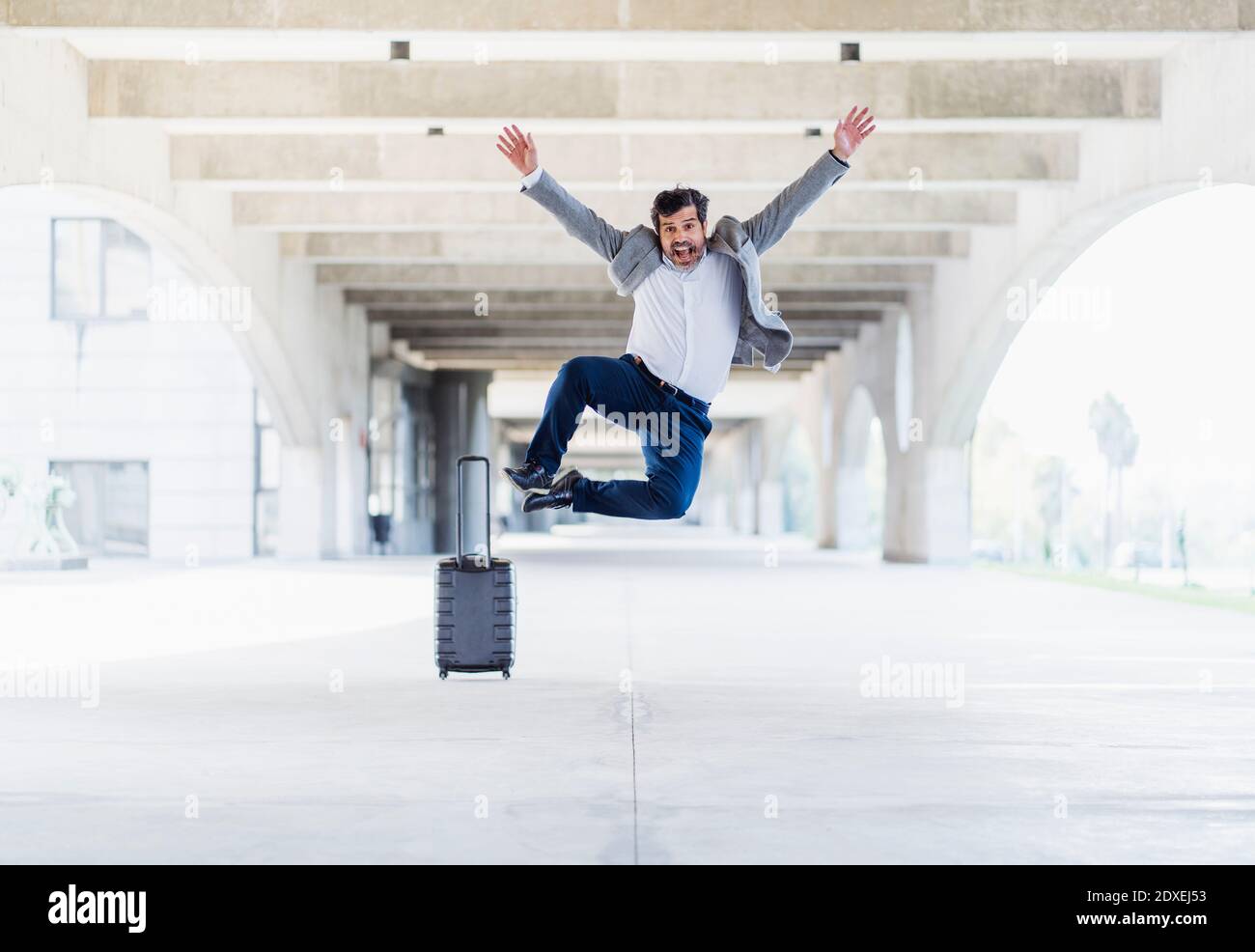 Happy male entrepreneur jumping with hands raised over concrete ...