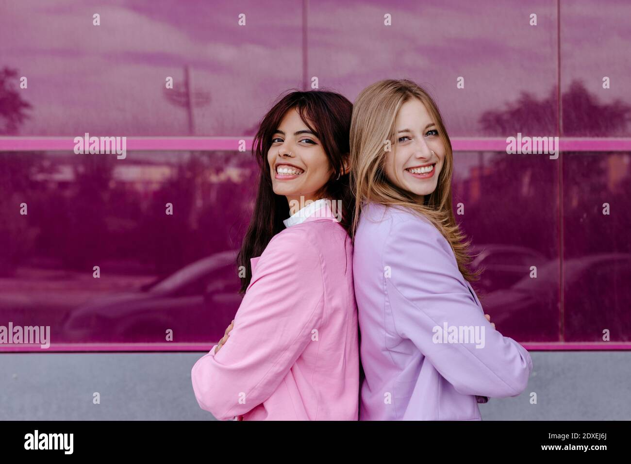Smiling sisters standing back to back by acrylic glass wall Stock Photo ...