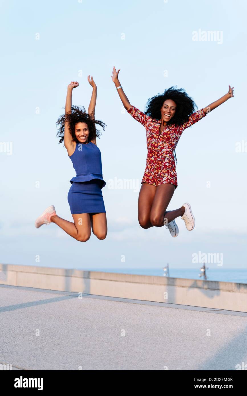 Cheerful female friends jumping at rooftop of building Stock Photo - Alamy