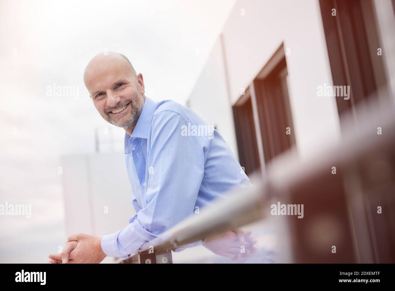 Businessman smiling while leaning on railing at rooftop Stock Photo - Alamy