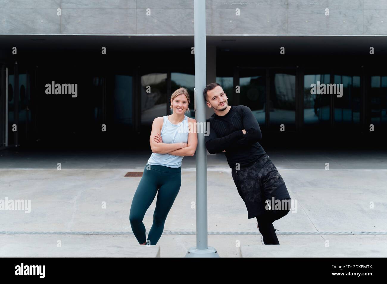 Smiling young couple leaning on pole Stock Photo - Alamy