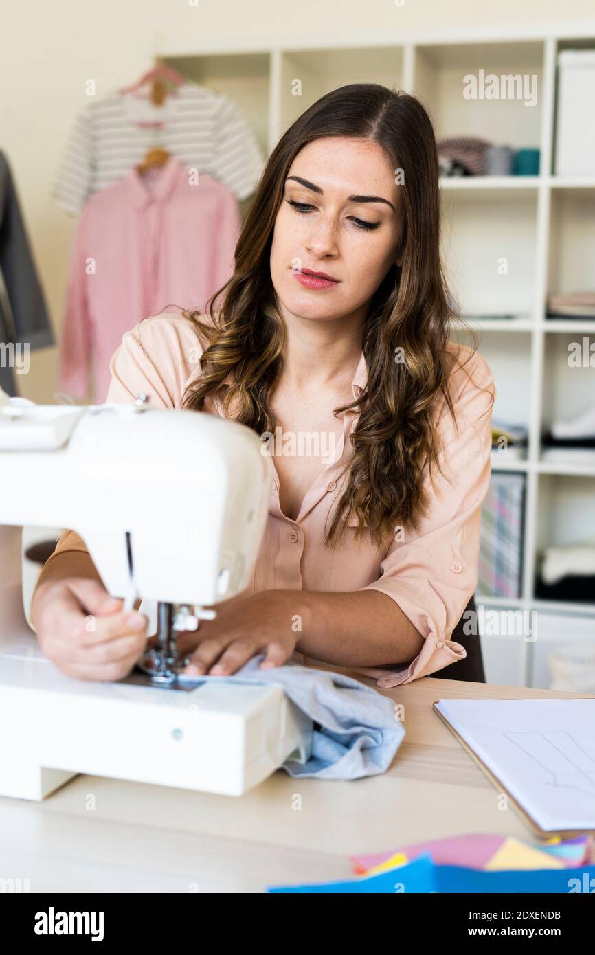 Young female designer using sewing machine while sitting at studio ...