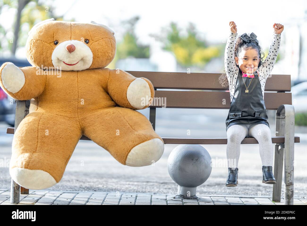 Happy girl with hand raised sitting by teddy bear at social distance on ...