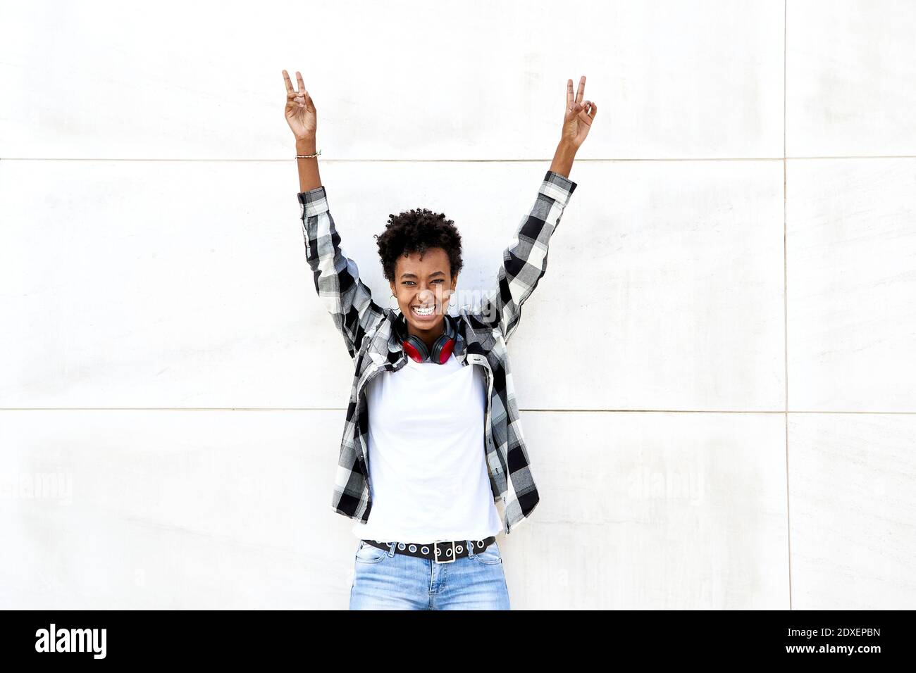 Cheerful female Afro hipster showing peace sign with arms raised ...