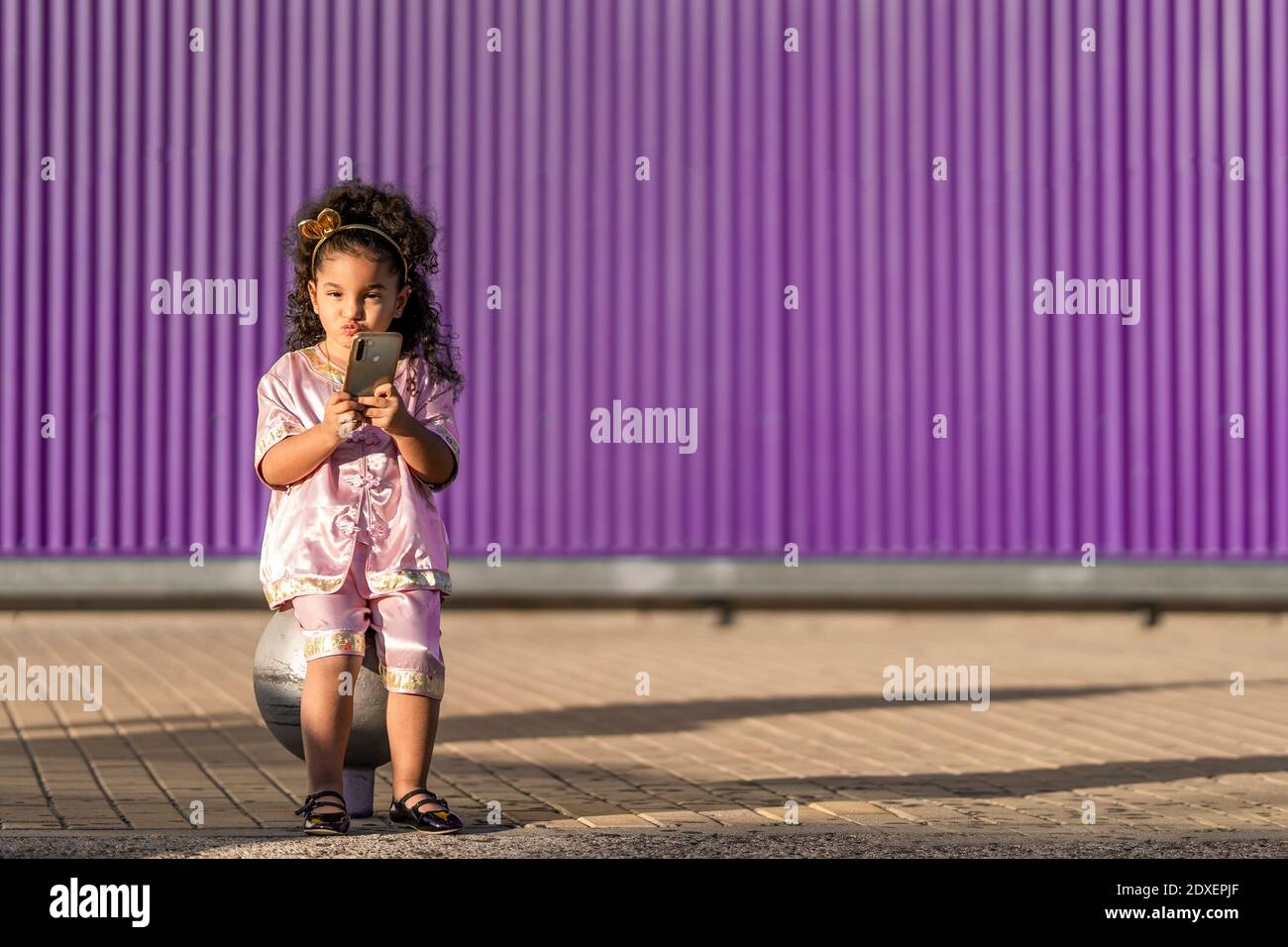 Cute girl doing pout while using mobile phone against purple wall Stock ...
