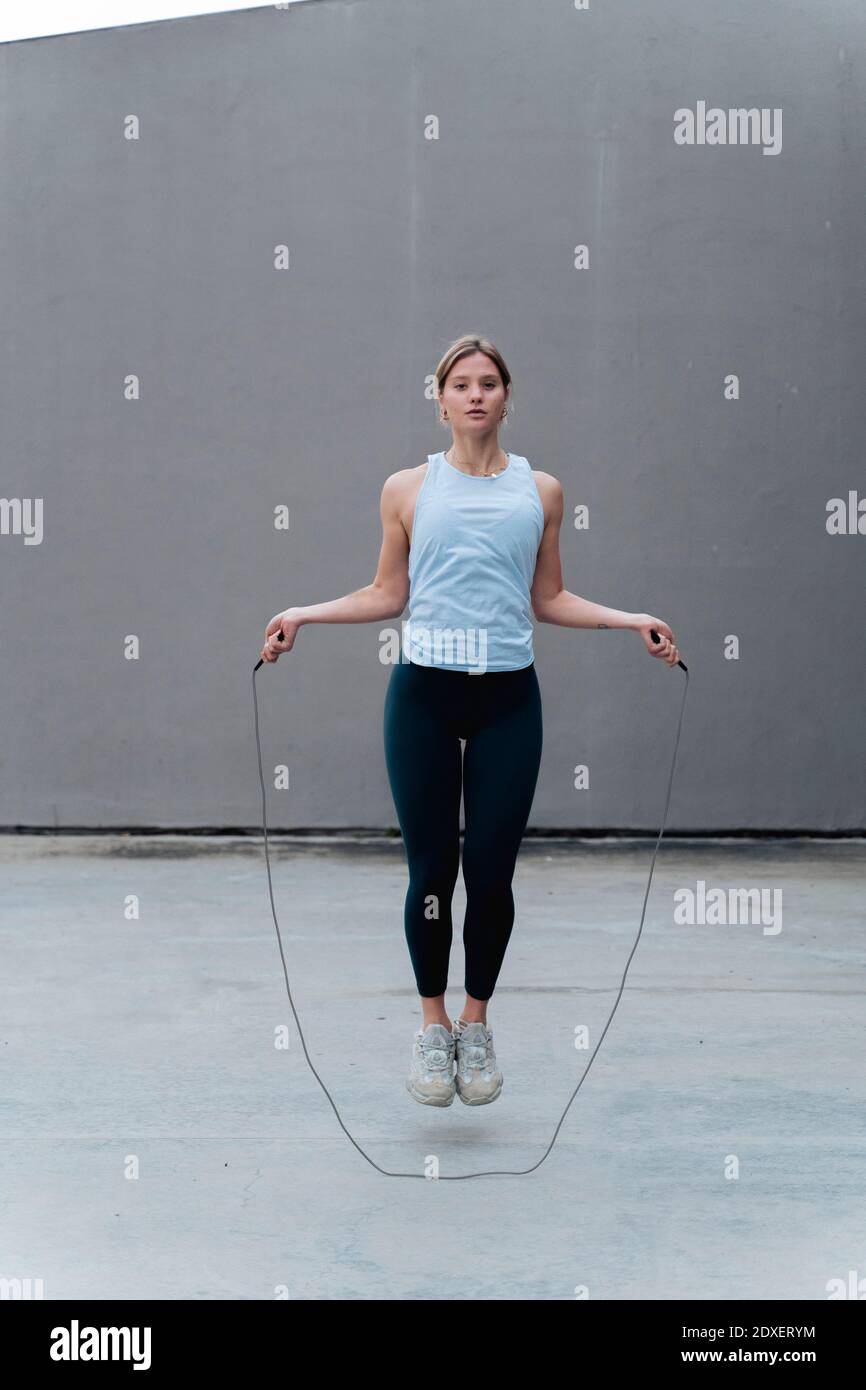 Young woman skipping rope while standing against wall Stock Photo - Alamy