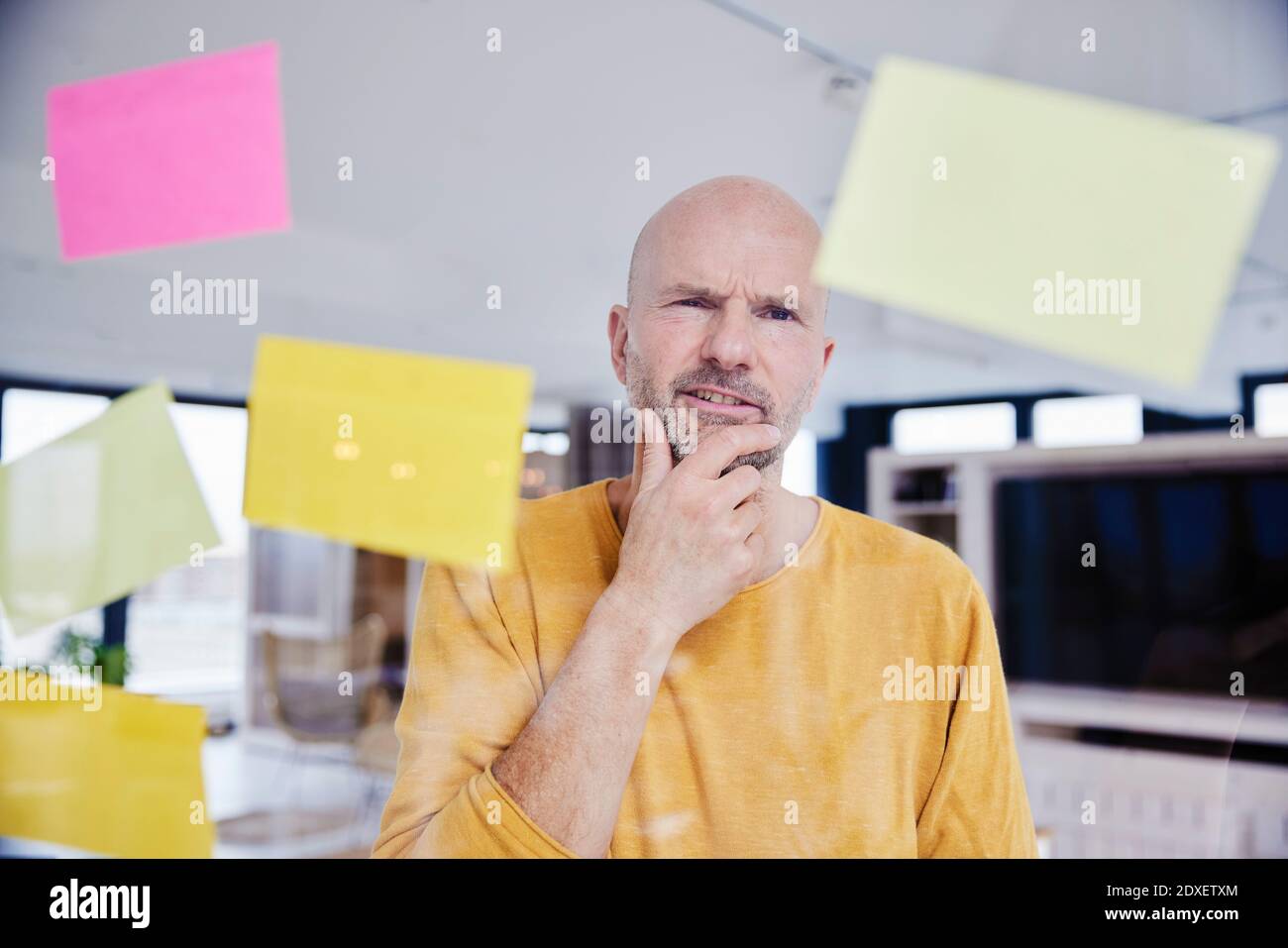 Confused man with hand on chin reading adhesive note Stock Photo - Alamy
