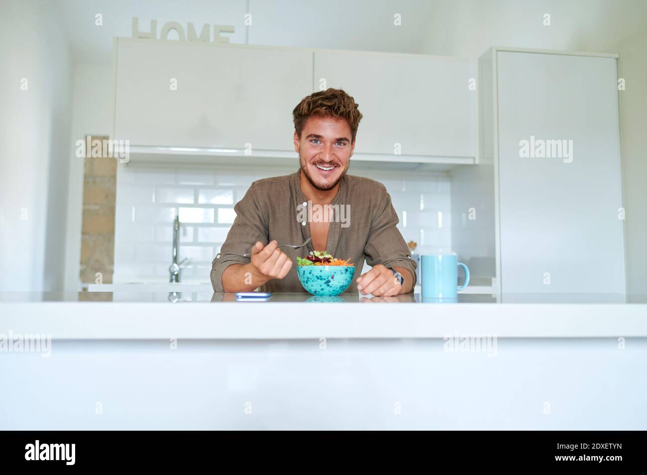 Smiling man with salad bowl leaning over kitchen counter at home Stock ...