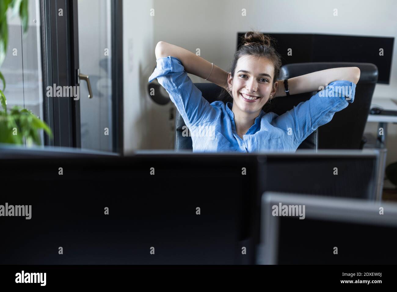 Smiling businesswoman sitting with hands behind head on chair at office ...
