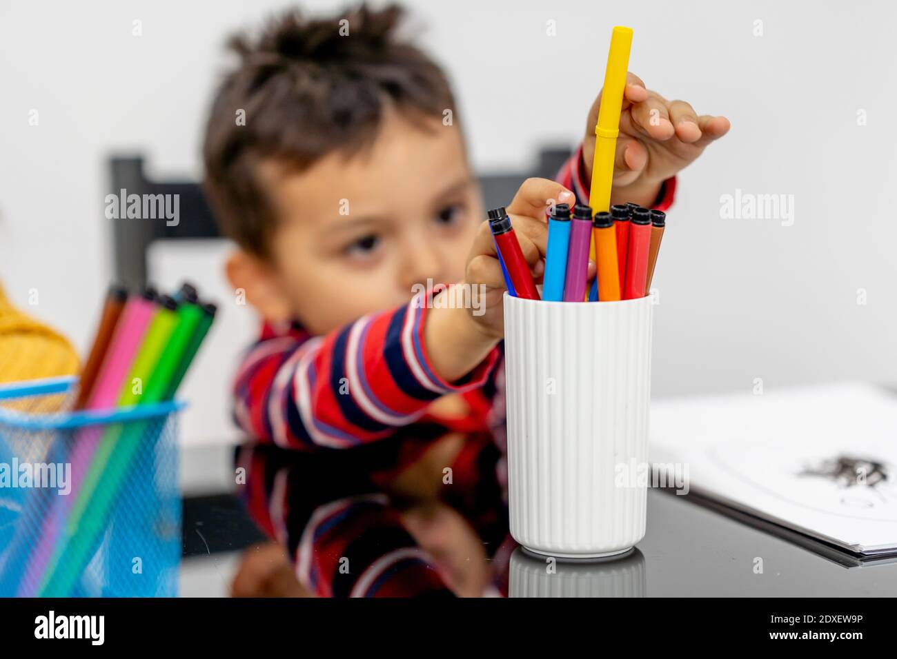 Boy removing sketch pen from desk organizer while learning drawing at ...