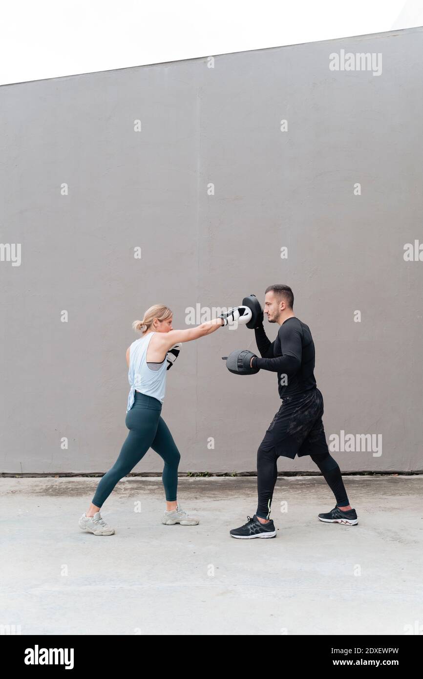 Sportsman teaching boxing to woman while standing against wall Stock ...