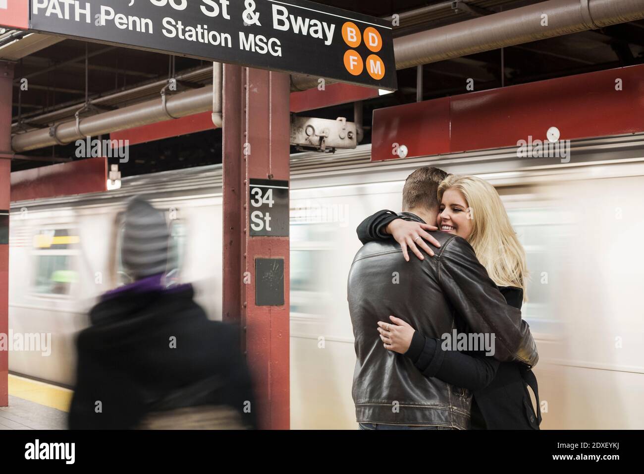 Girlfriend smiling while embracing boyfriend standing at subway station ...