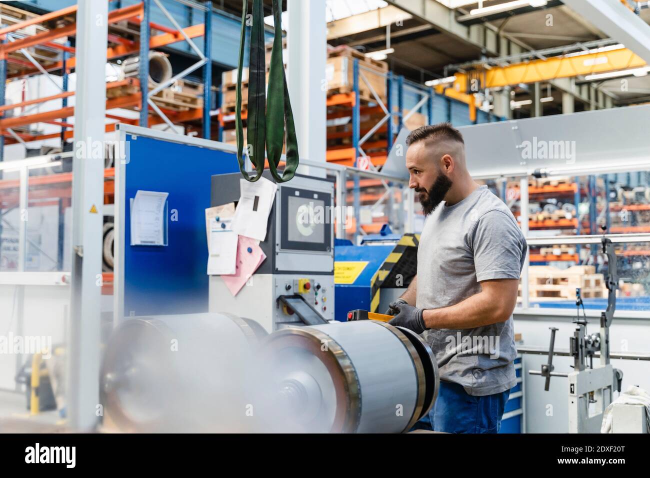 Male technician examining machine while standing at illuminated factory ...