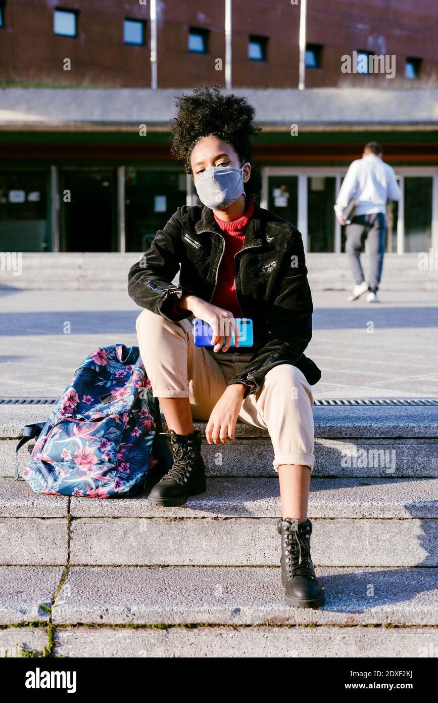 Young woman wearing protective face mask sitting on staircase in city ...