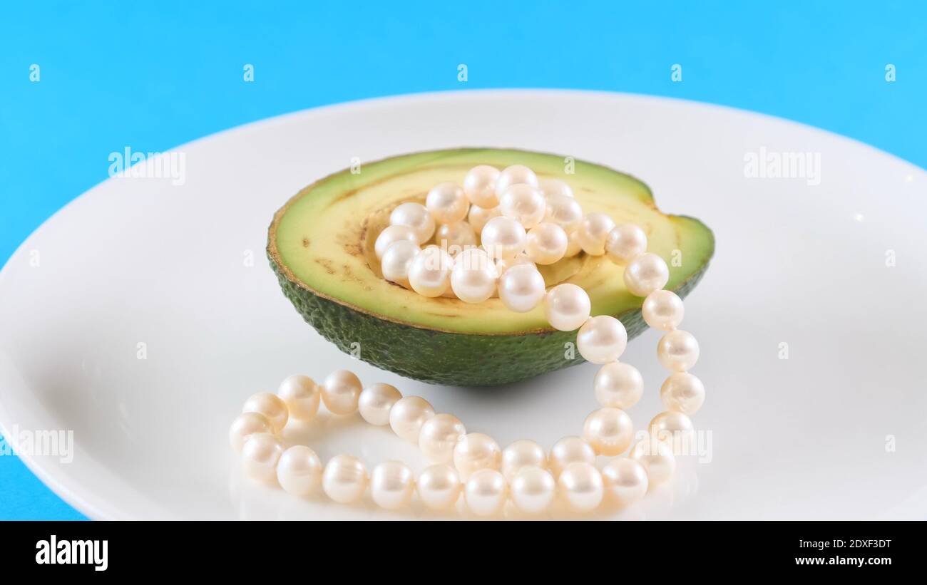 half an avocado with pearls on white plate on a blue background ...