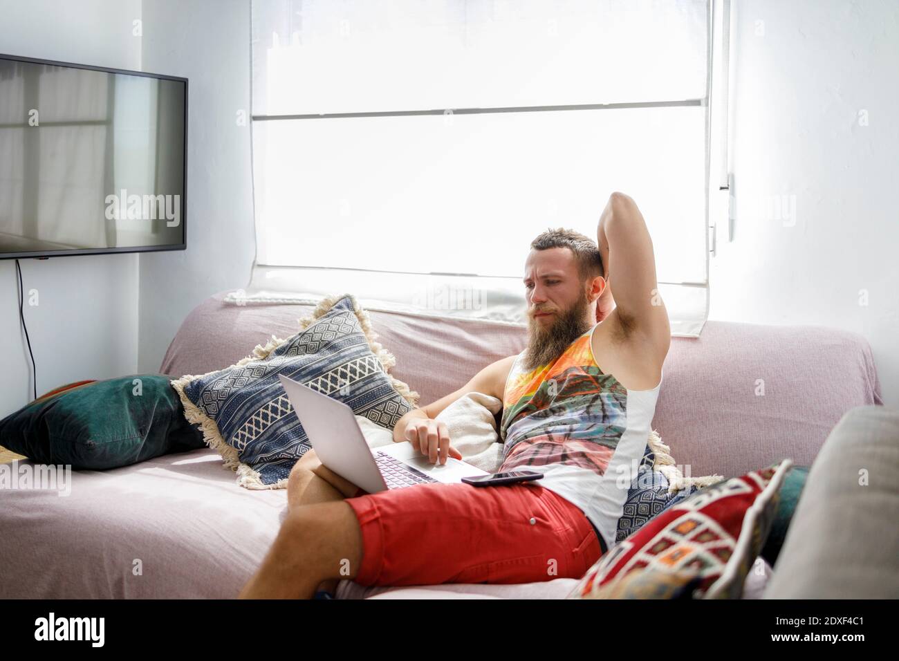 Bearded Man Using Laptop While Sitting On Sofa In Living Room Stock