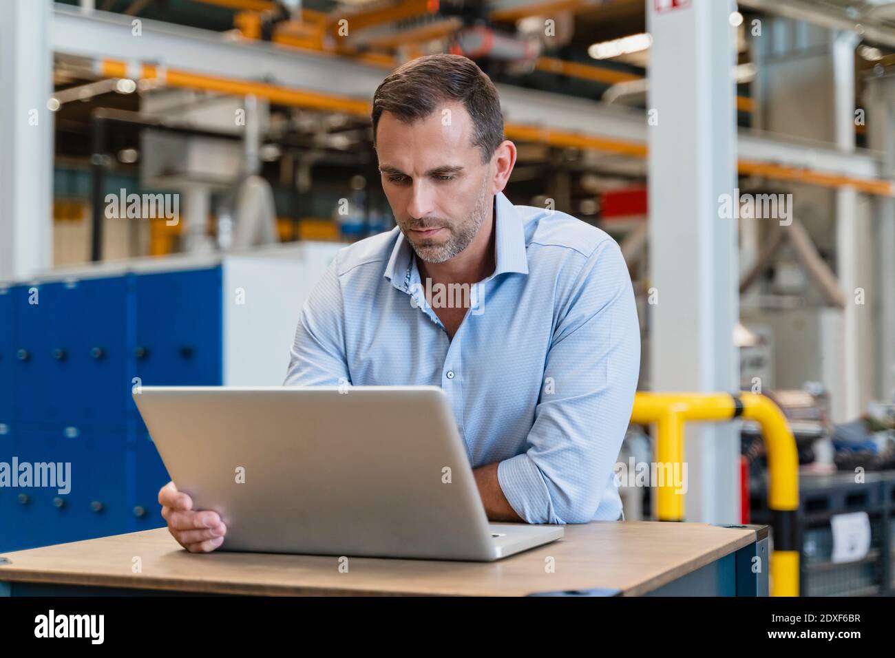 Male entrepreneur using laptop while leaning on desk in factory Stock ...