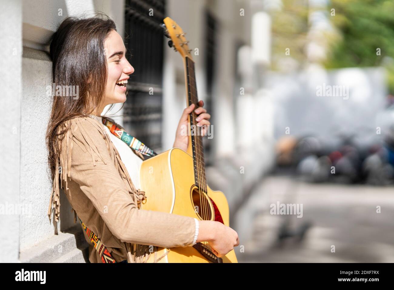 Female musician laughing while playing guitar in city Stock Photo - Alamy