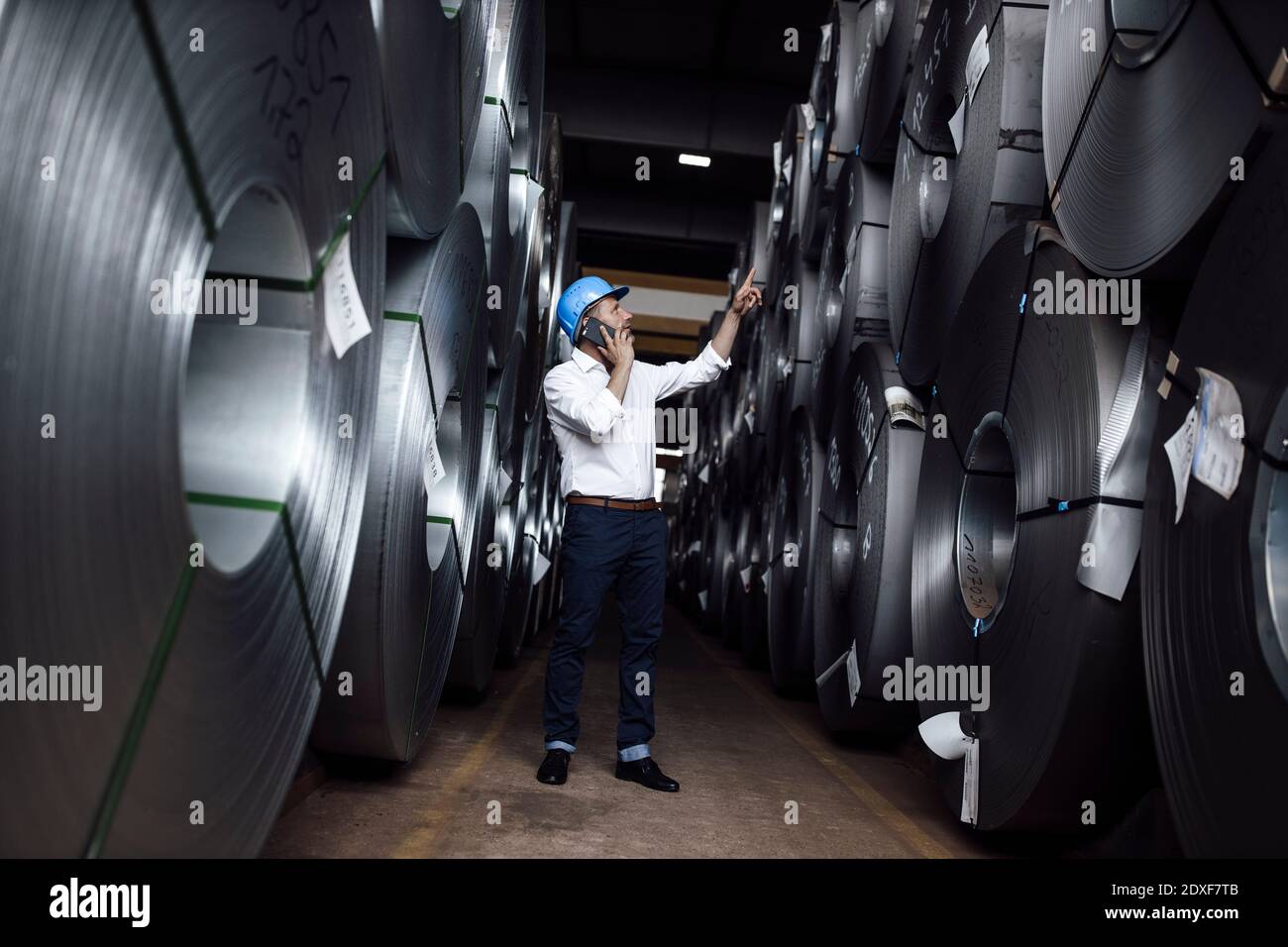 Male entrepreneur talking on smart phone while pointing on steel rolls ...