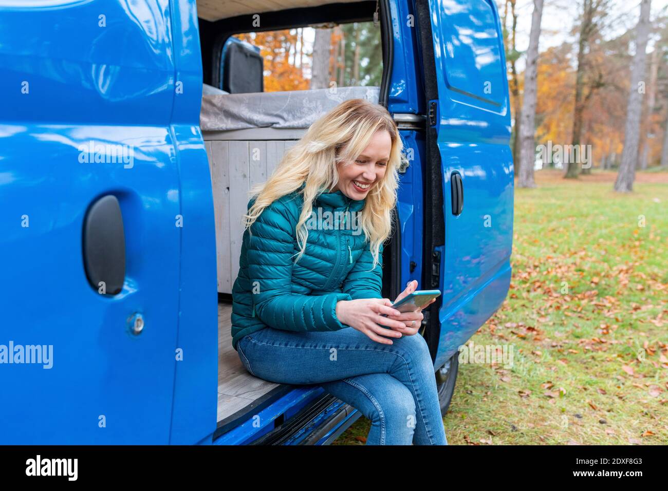 Happy woman using smart phone while siting at door of camper van Stock ...