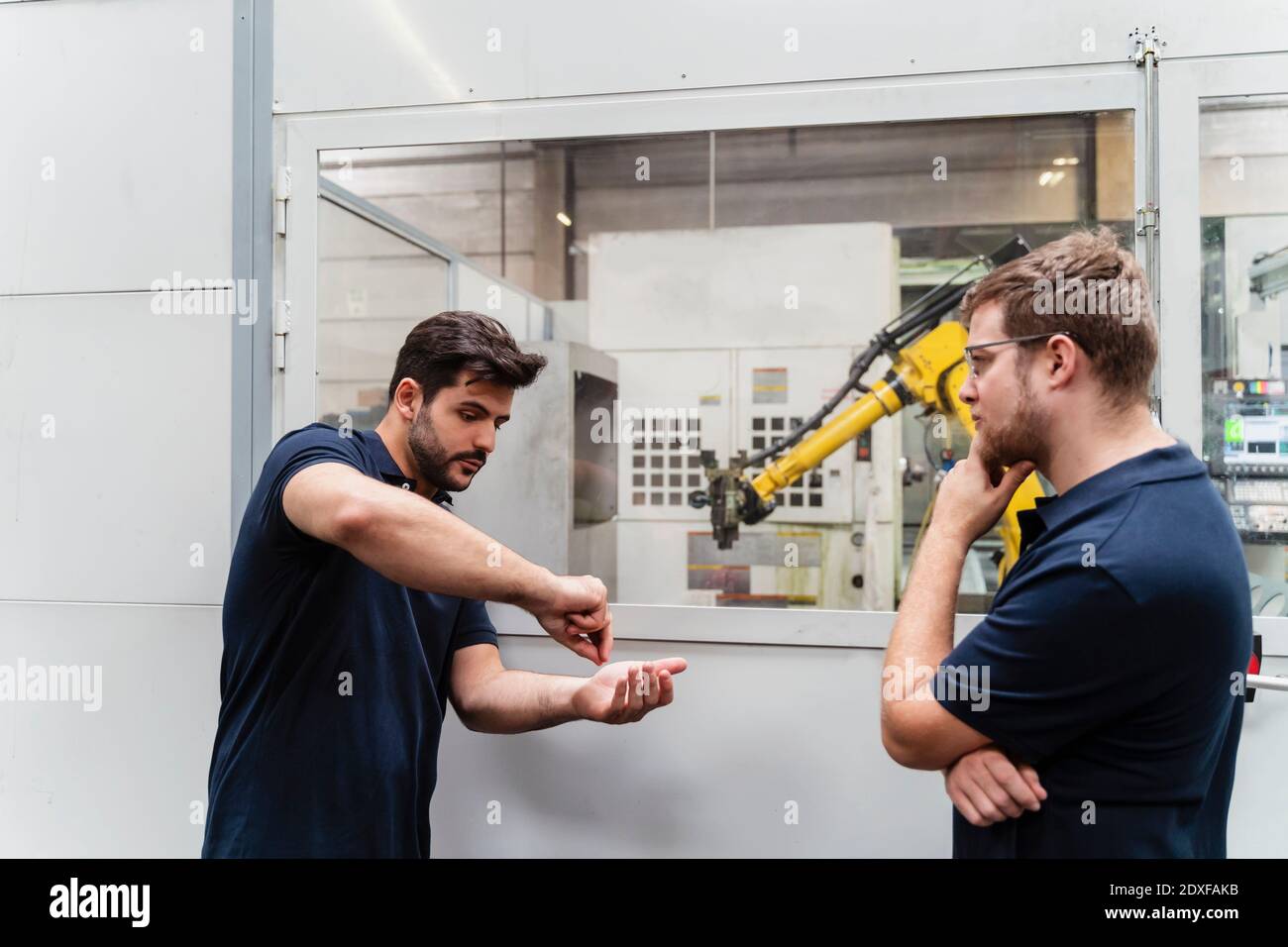 Young male worker explaining to coworker while standing in industry ...