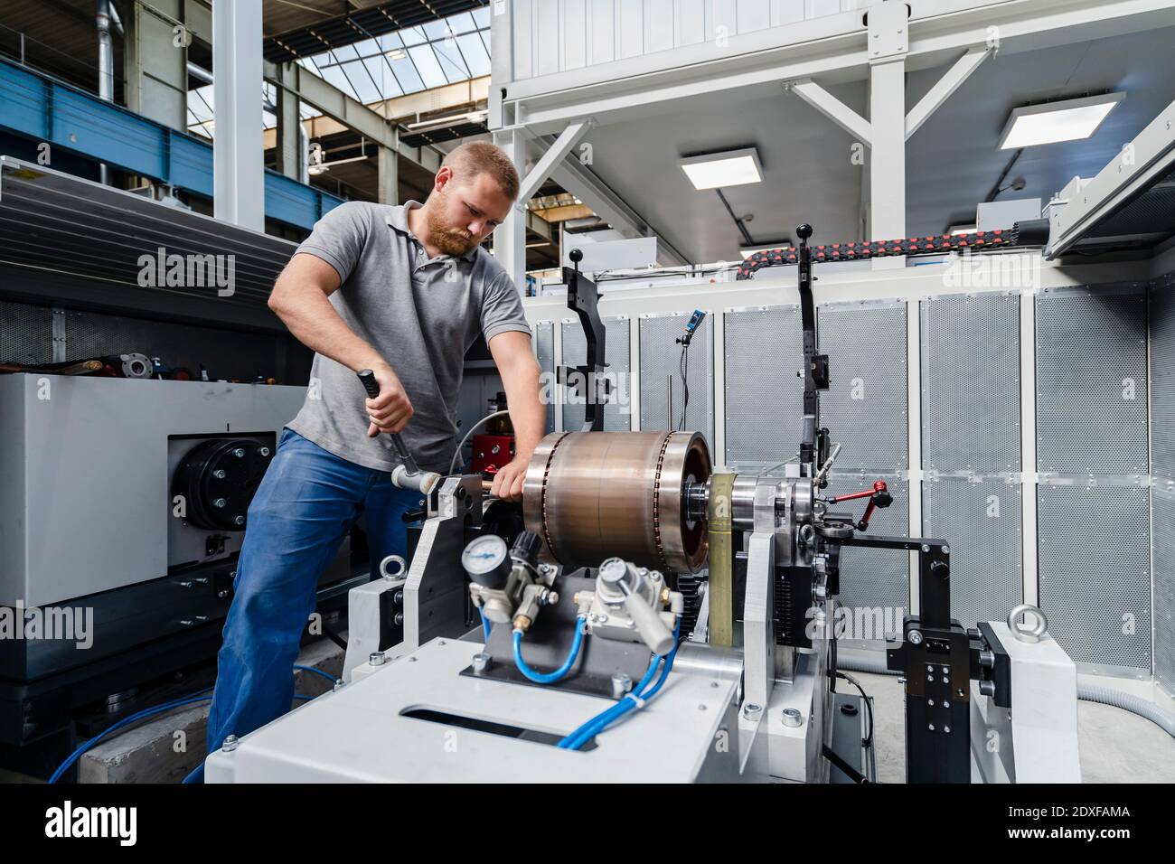 Manual worker tightening bolt of machine while standing at factory ...