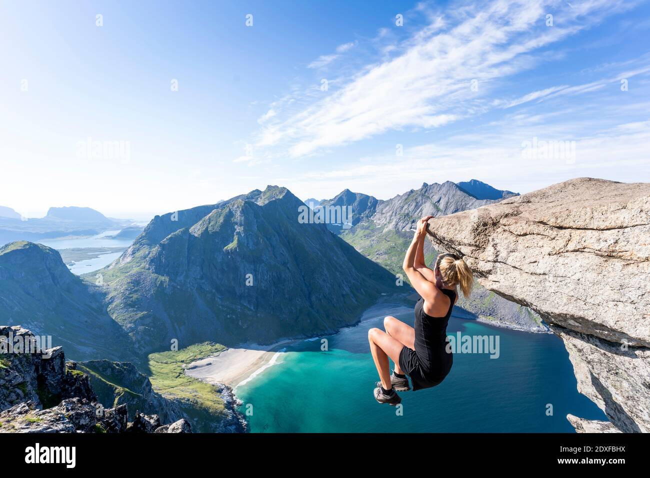 Mid adult woman hanging on edge of mountain at Ryten, Lofoten, Norway ...