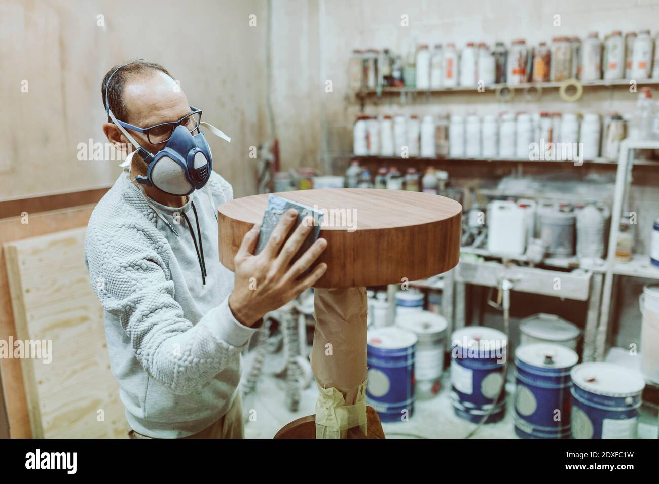 Carpenter wearing protective face mask rubbing table with sand paper ...