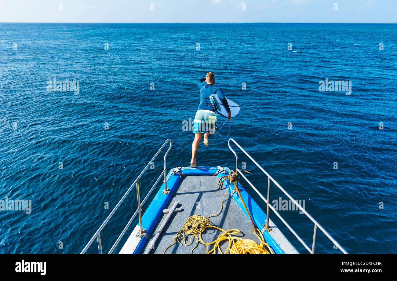 Male surfer with surfboard jumping in sea from boat deck Stock Photo ...