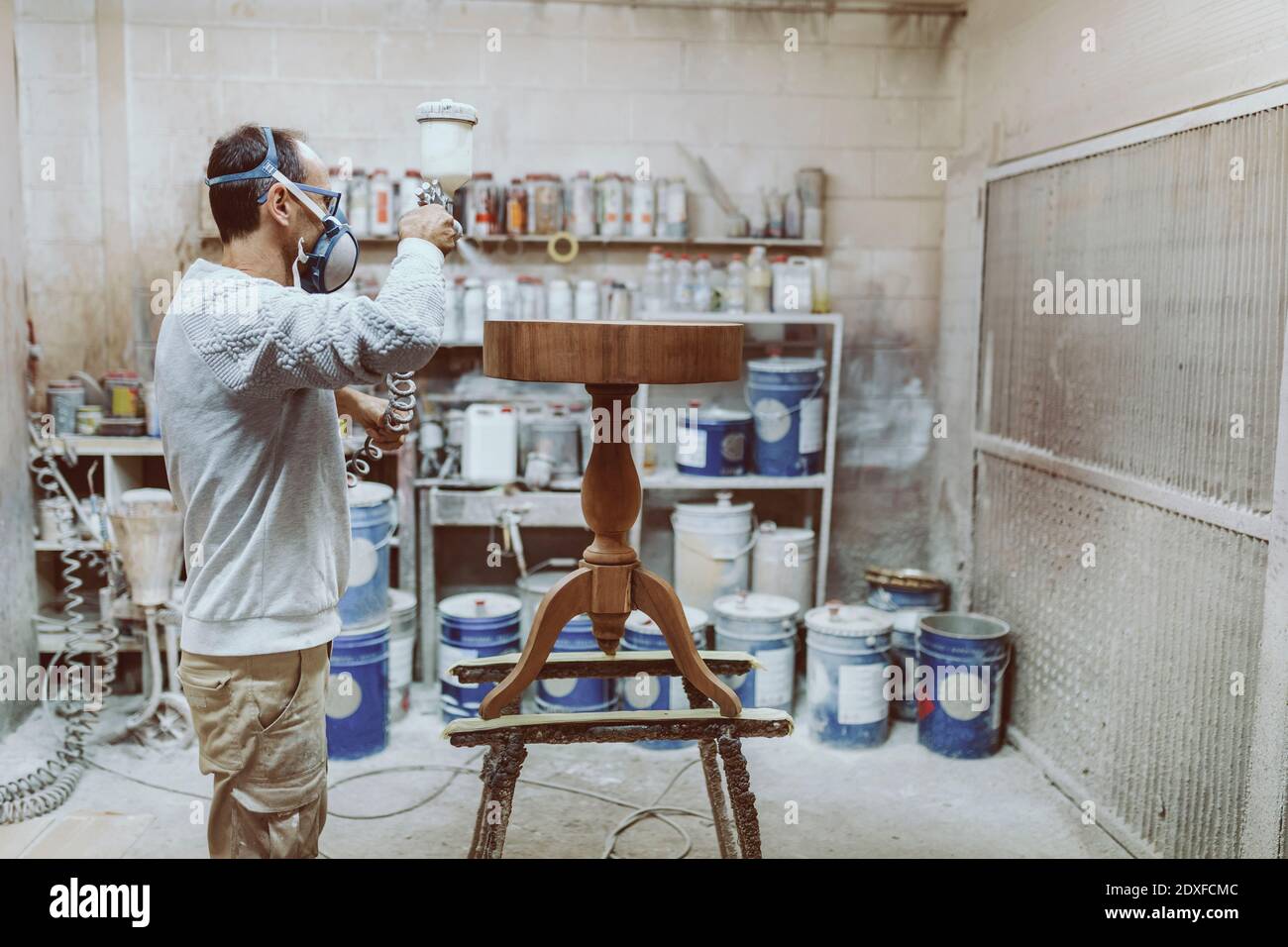 Manual worker wearing protective face mask spraying on table while ...