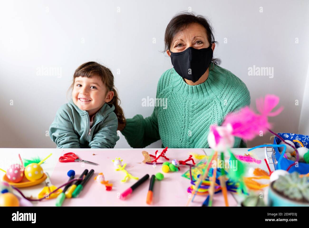 Grandmother wearing protective face mask sitting with granddaughter ...