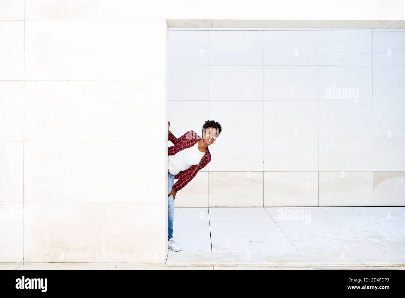 Happy young woman standing behind white wall Stock Photo - Alamy