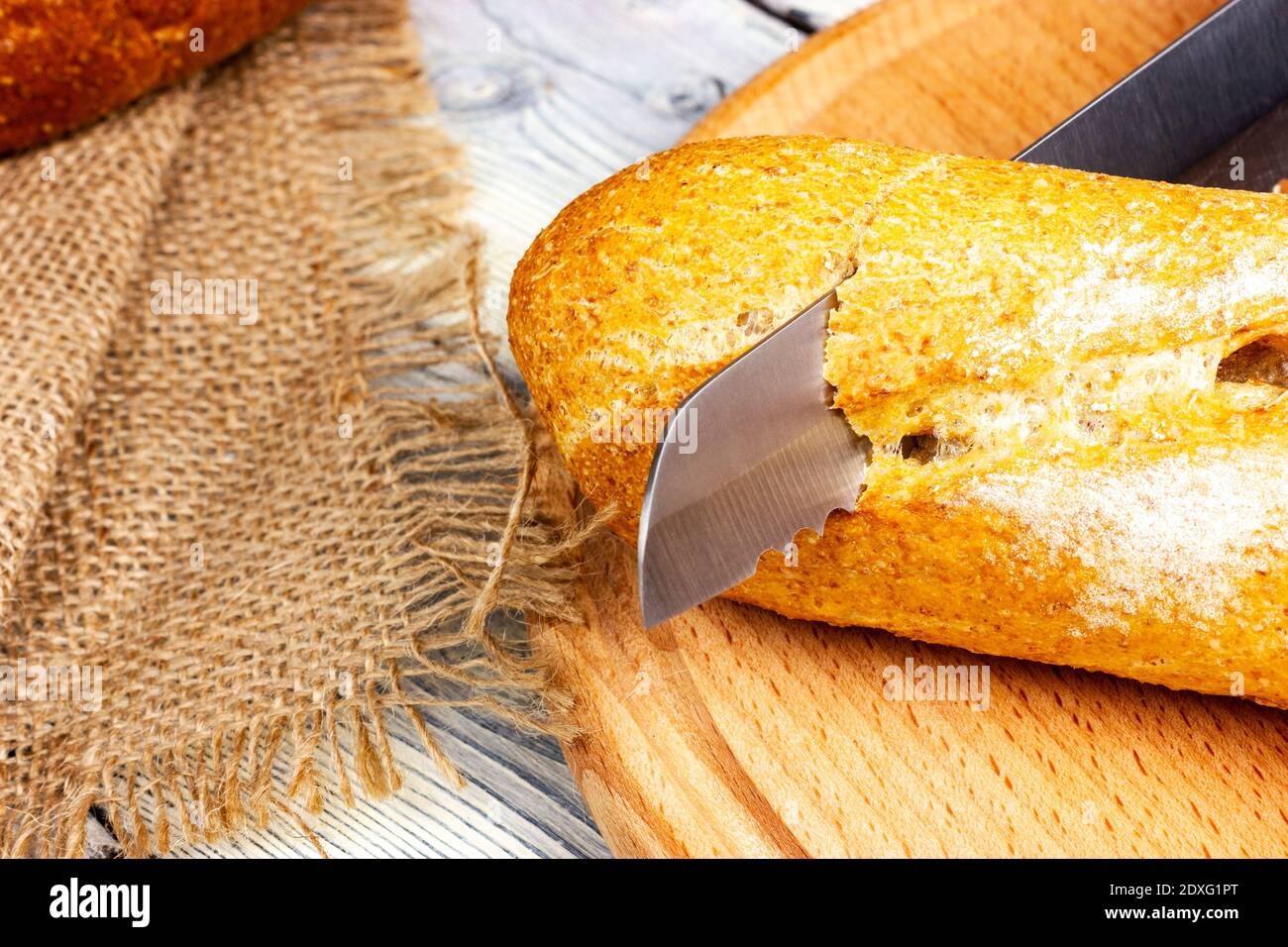 A bread knife cuts a fresh French baguette. White bread. Cutting bread ...