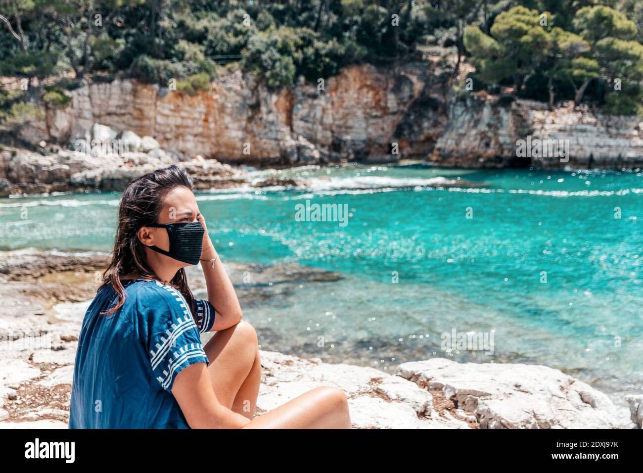 A shallow focus closeup of a female sitting on the rocky coastal area ...