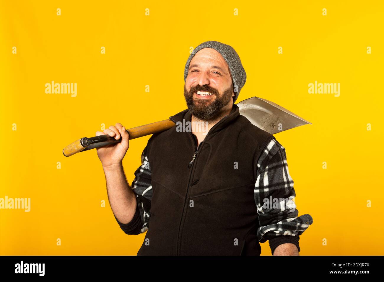 Portrait of an adult worker man with a shovel on his shoulder against a ...