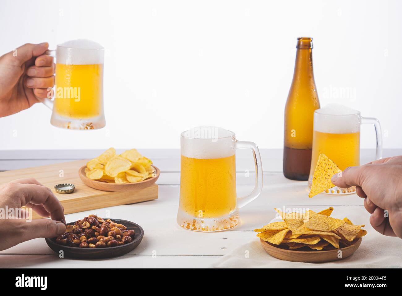 Hands holding beer and sharing a snack on white wooden base and white ...