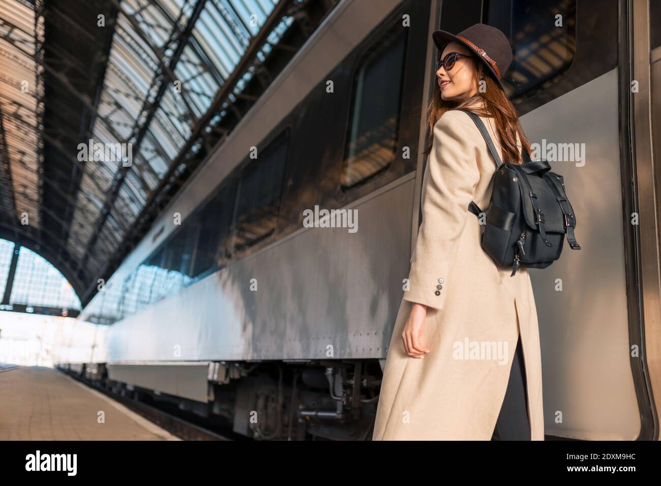 Beautiful traveler with backpack on the platform of the railway station. Young woman near train ...